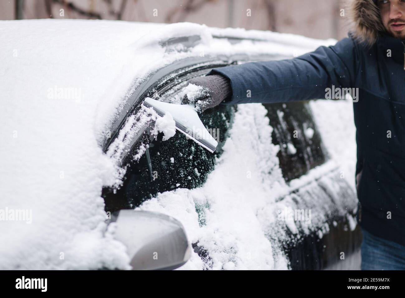 Close up of man is cleaning snowy window on a car with snow scraper ...