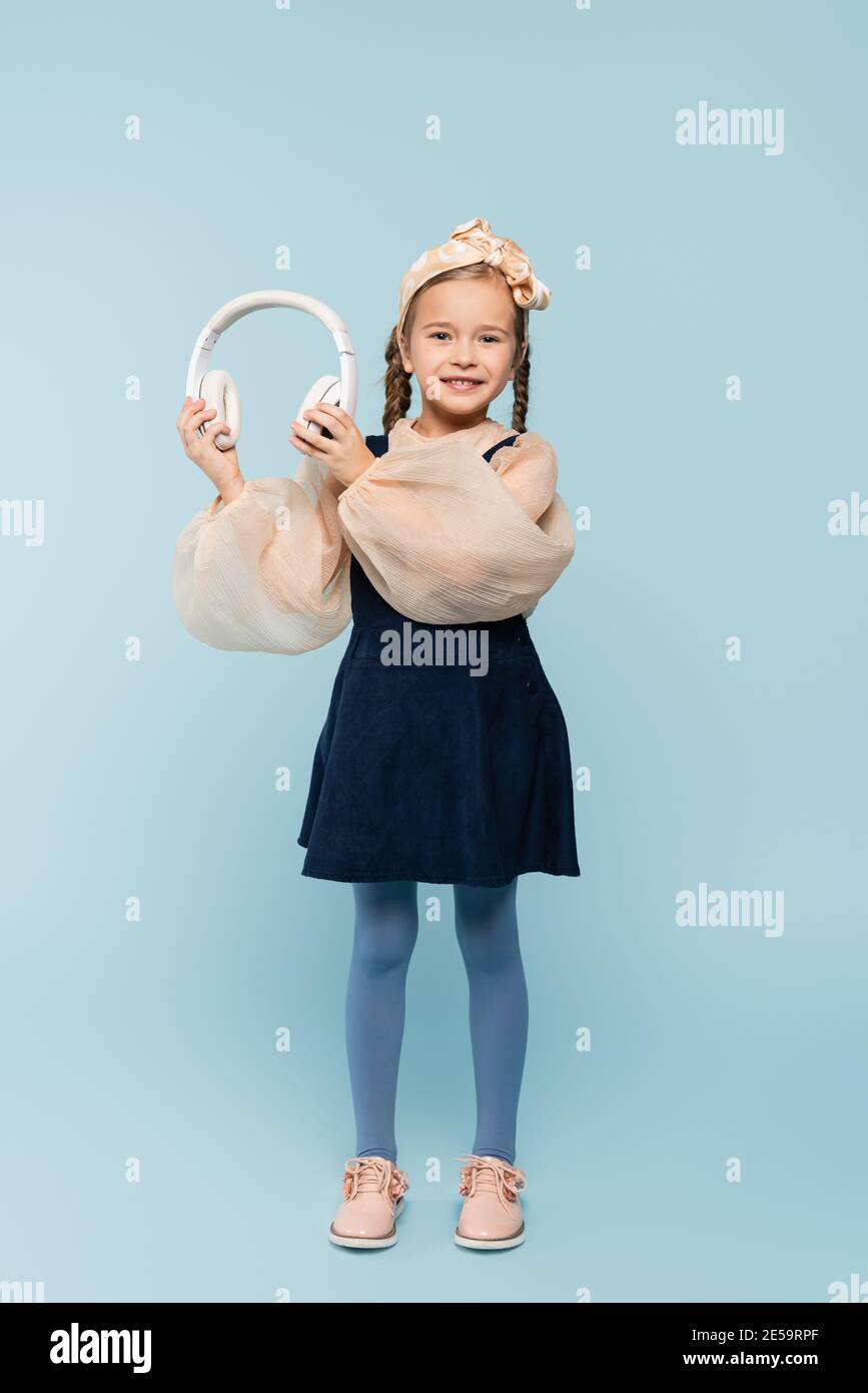 full length of cheerful kid in headband with bow holding wireless ...
