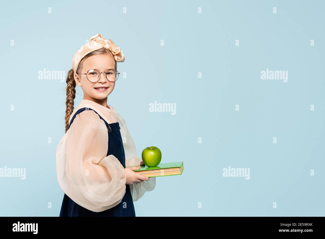 smart kid in glasses smiling while holding book and green apple ...