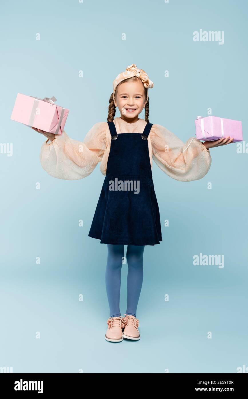 full length of happy kid with pigtails holding presents on blue Stock ...