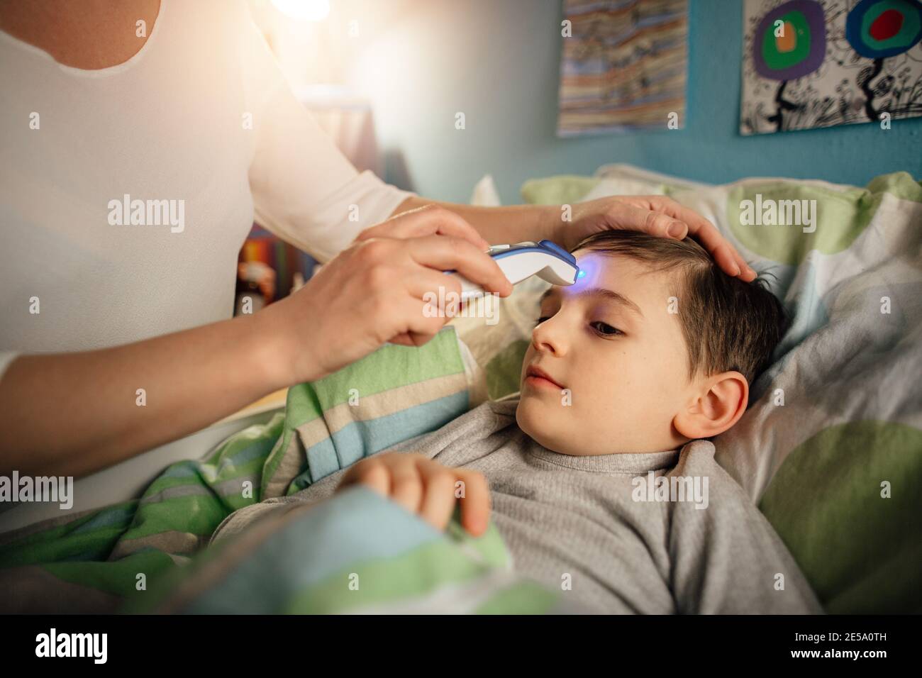 A mother taking a temperature of her sick child lying in bed. A young ...