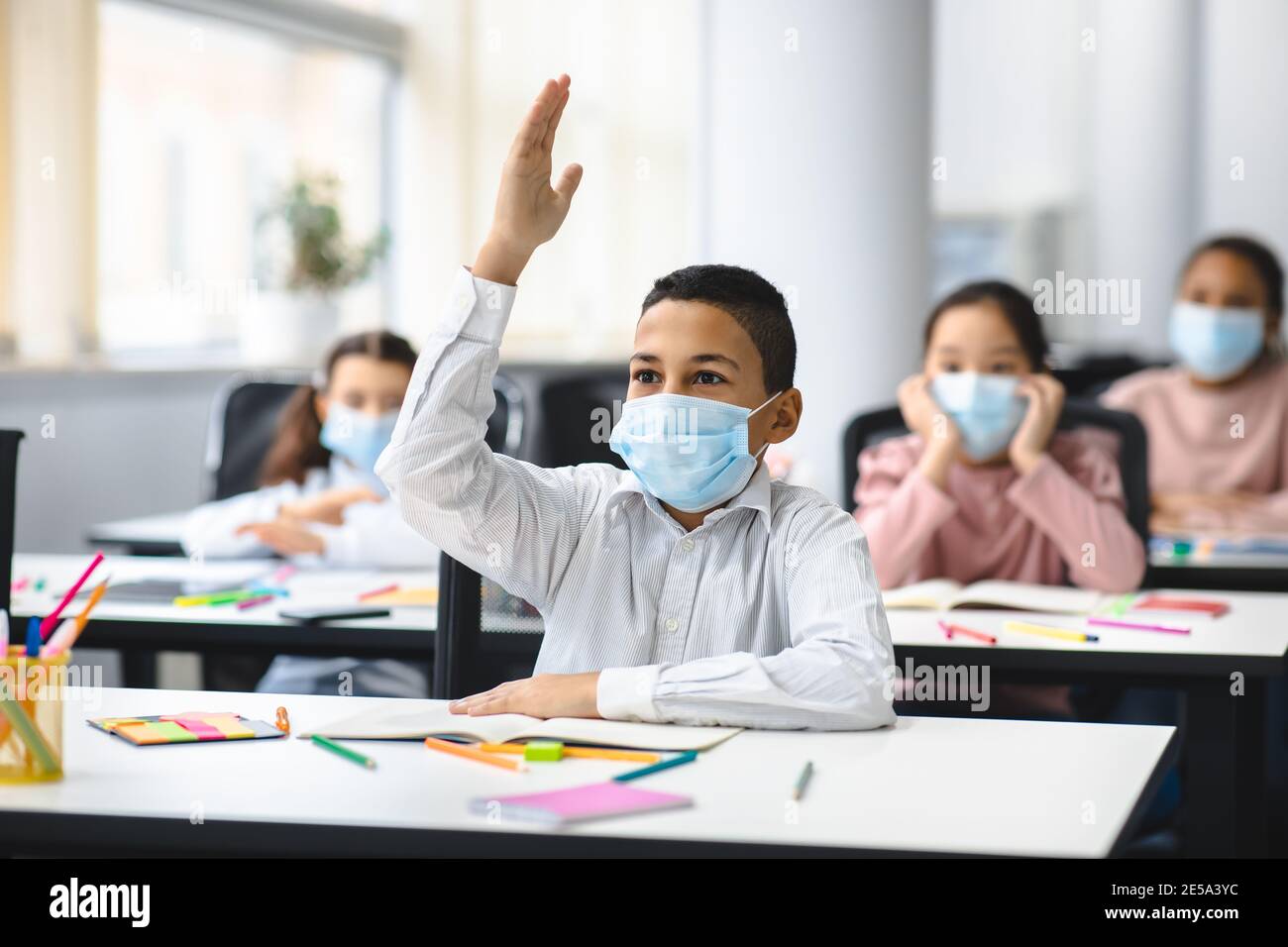 Boy raising hand at classroom, wearing medical mask Stock Photo - Alamy