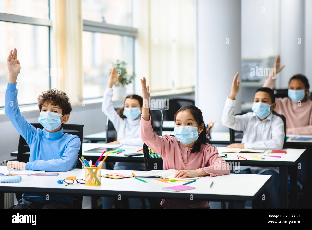 Schoolchildren raising hands at classroom, wearing medical masks Stock ...