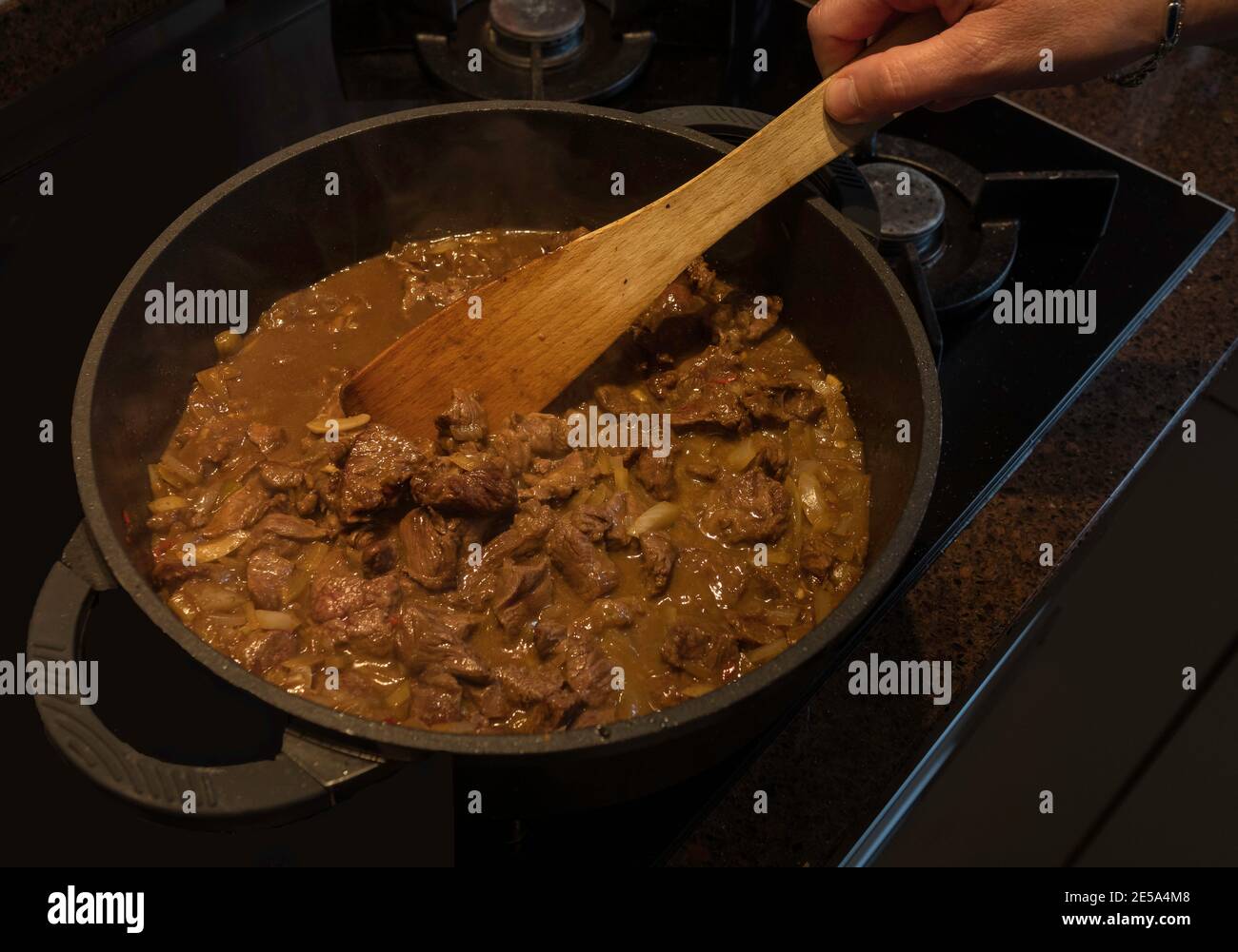 woman stirs in a pan with while making a beef stew daging smoor in the ...