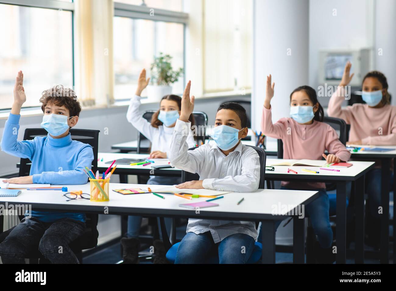Schoolchildren raising hands at classroom, wearing medical masks Stock ...