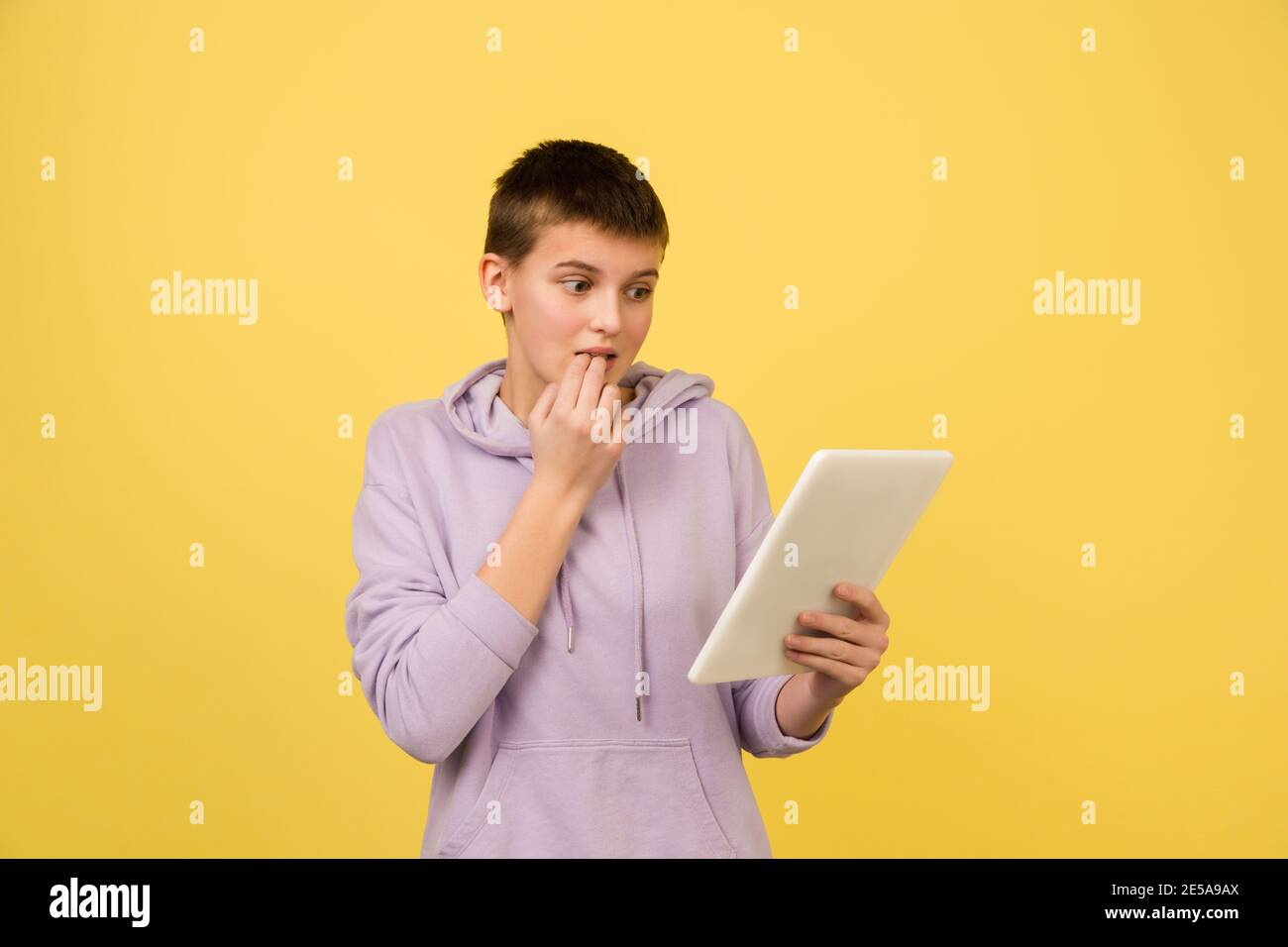 Scared scrolling tablet. Caucasian girl's portrait isolated on yellow ...