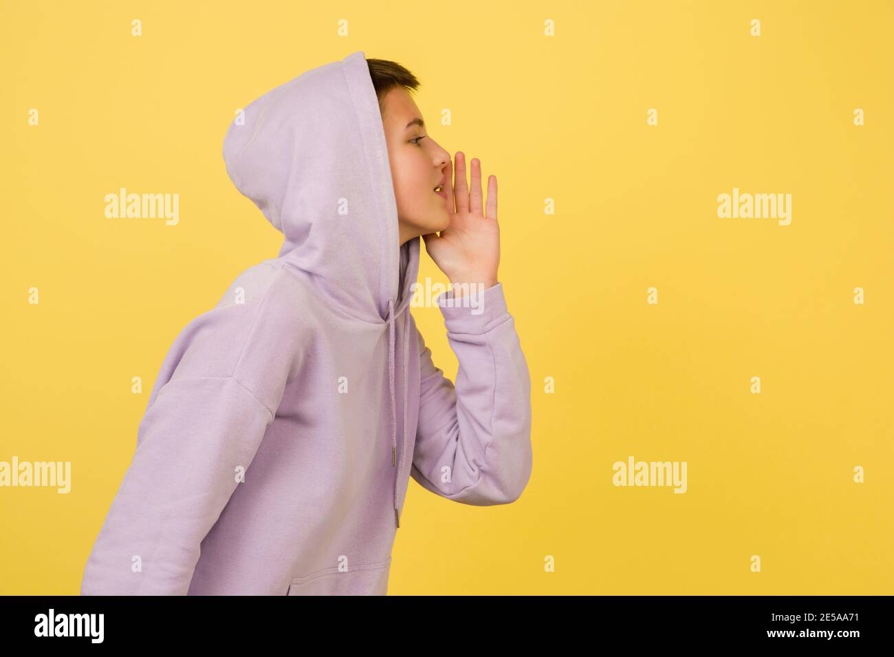 Whispering secretly. Caucasian girl's portrait isolated on yellow ...