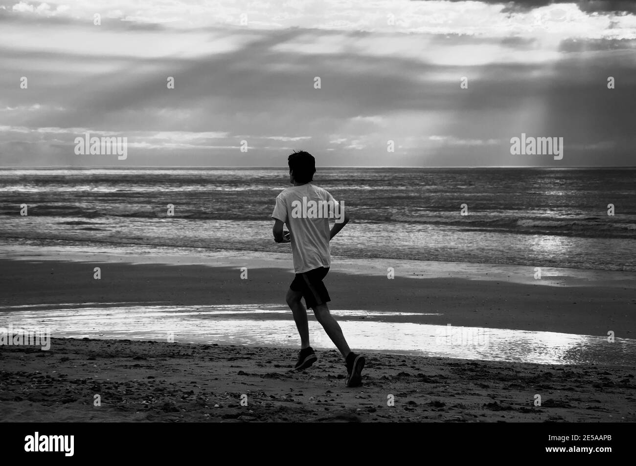 Young man running on beach at sunset. Back view. Dramatic sky lighting ...