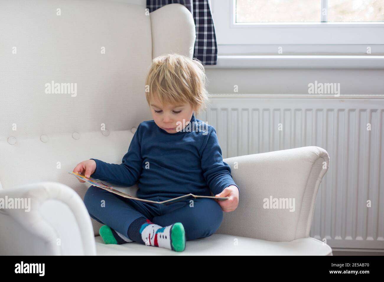 Mother and child, toddler boy, reading a book, sitting in a cozy ...