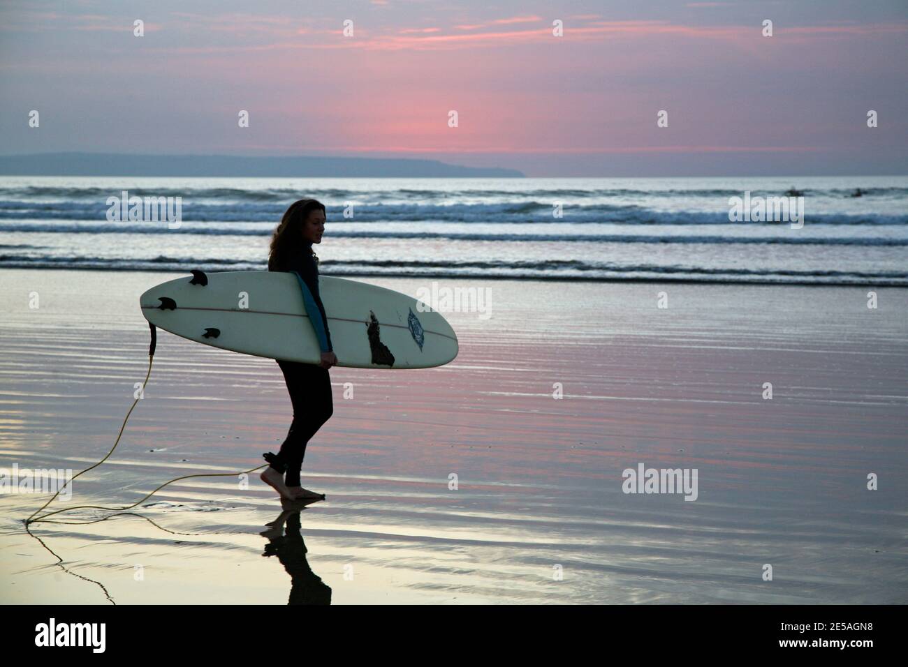 Female surfer with surfboard heading into the sea for an evening surf ...