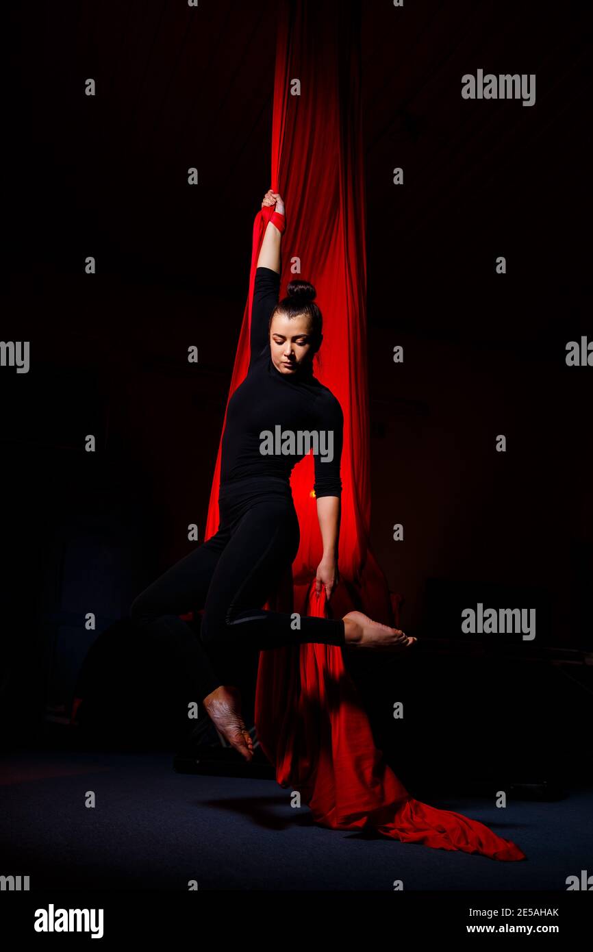 A sports girl performs gymnastic and circus exercises on red silk ...