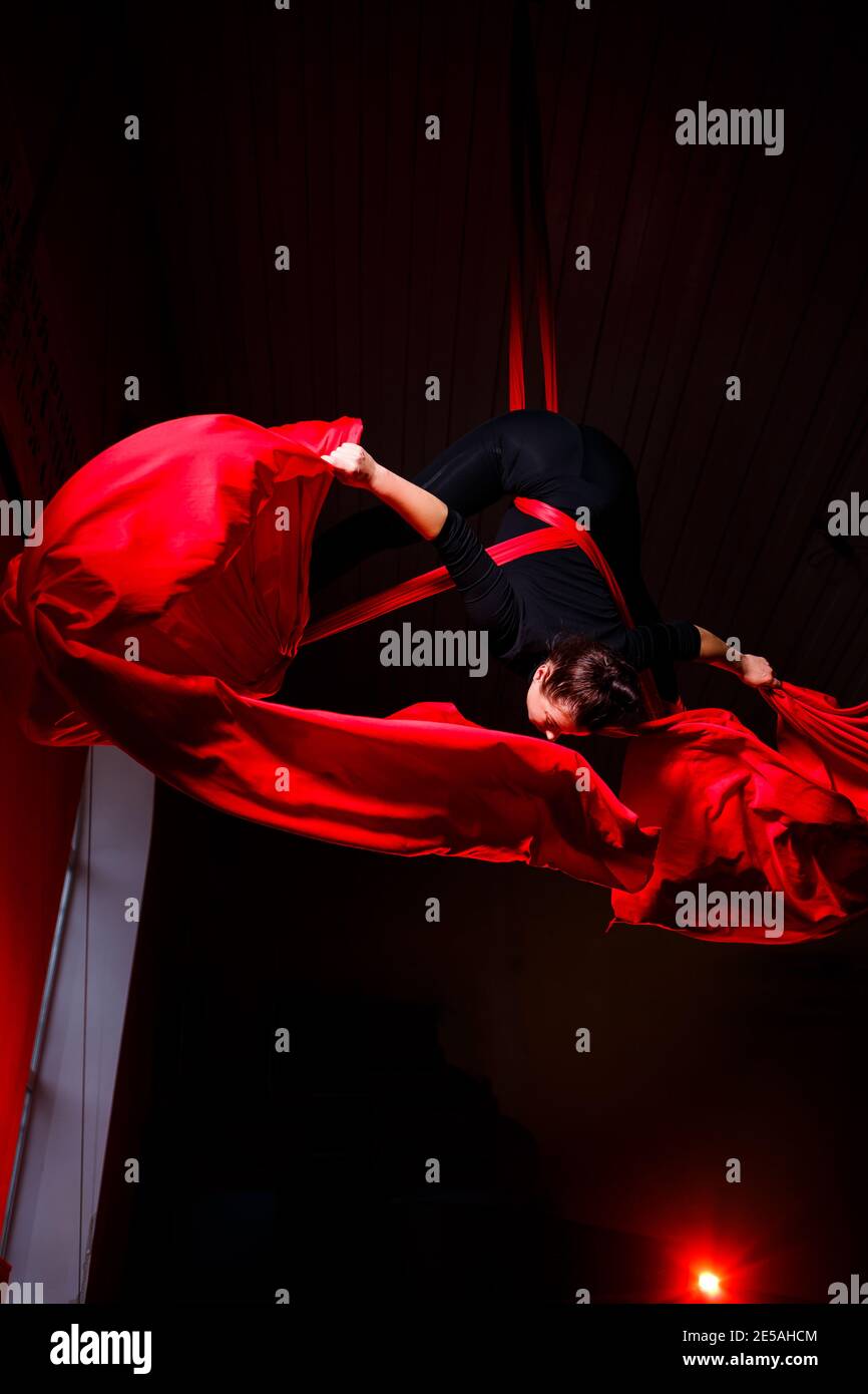 A sports girl performs gymnastic and circus exercises on red silk ...