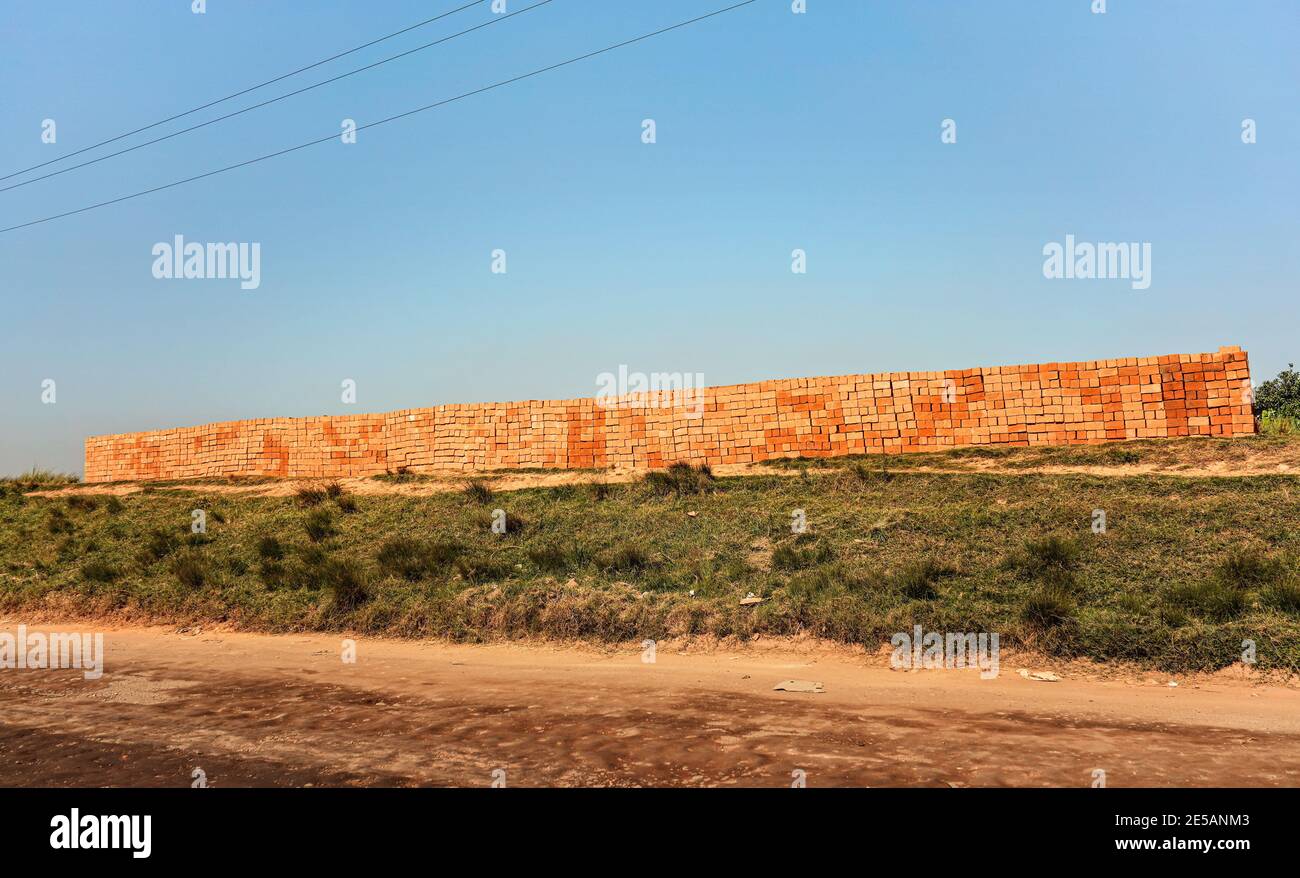 Orange red bricks made from local clay arranged in wide stack, ready ...