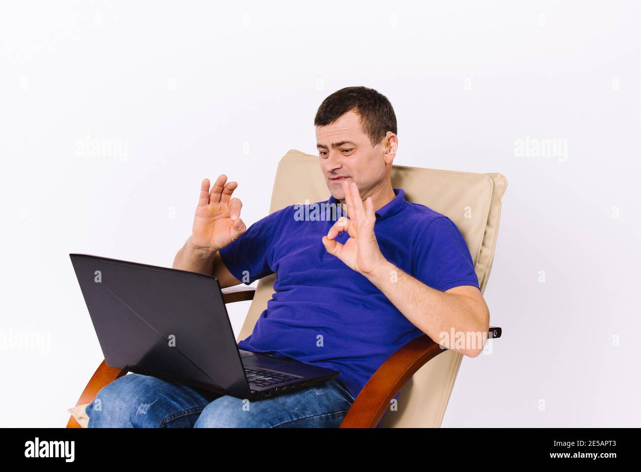 A deaf senior man with a laptop shows a sign to the camera that ...