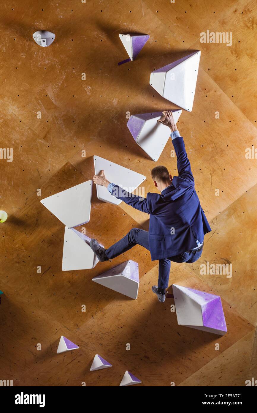 Young man in suit climbing difficult route on artificial wall in ...