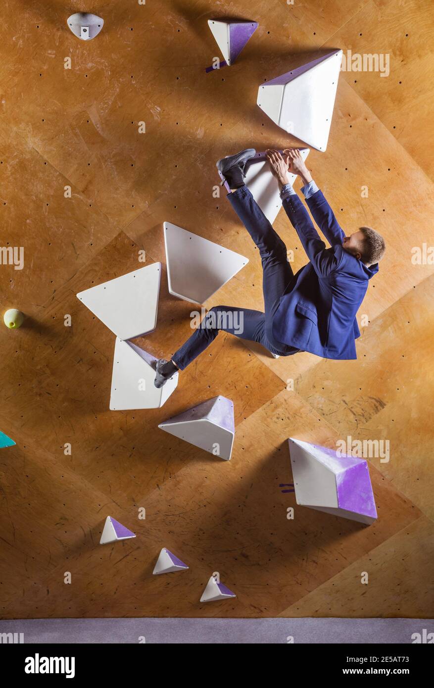 Young man in suit climbing difficult route on artificial wall in ...