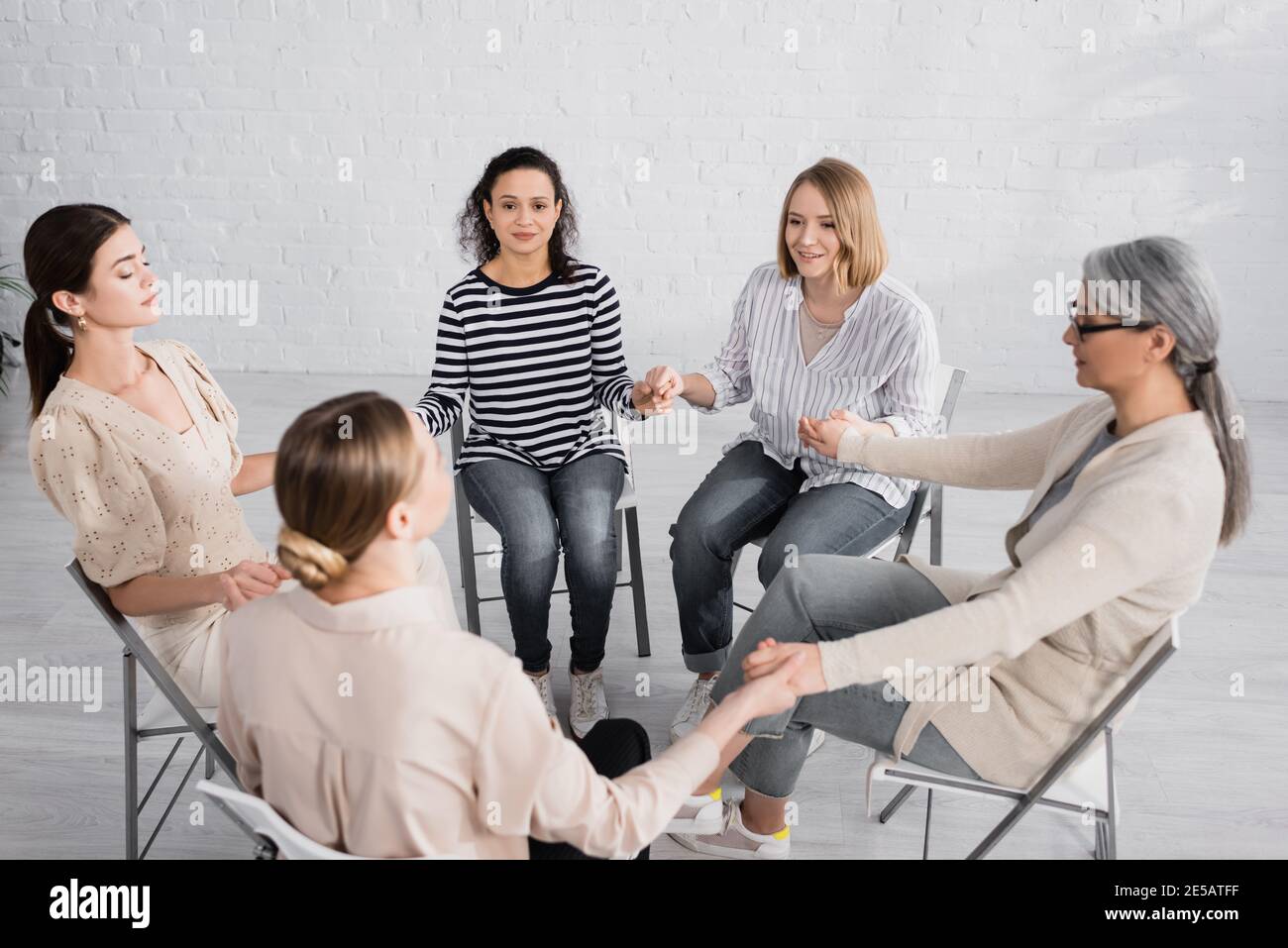 happy multicultural women smiling and holding hands during seminar ...