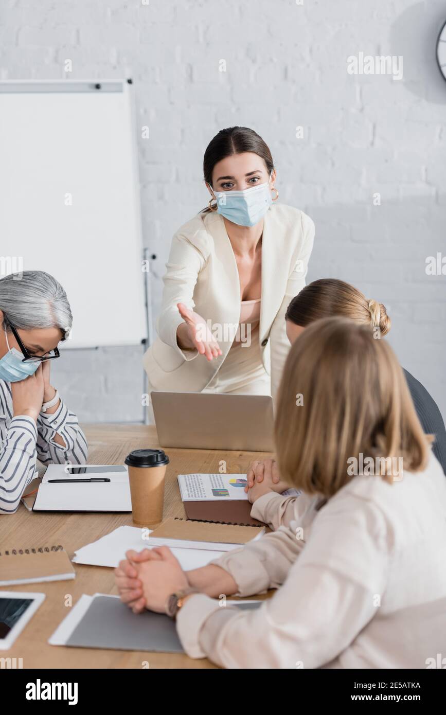 team leader in medical mask pointing with hand at businesswoman during ...
