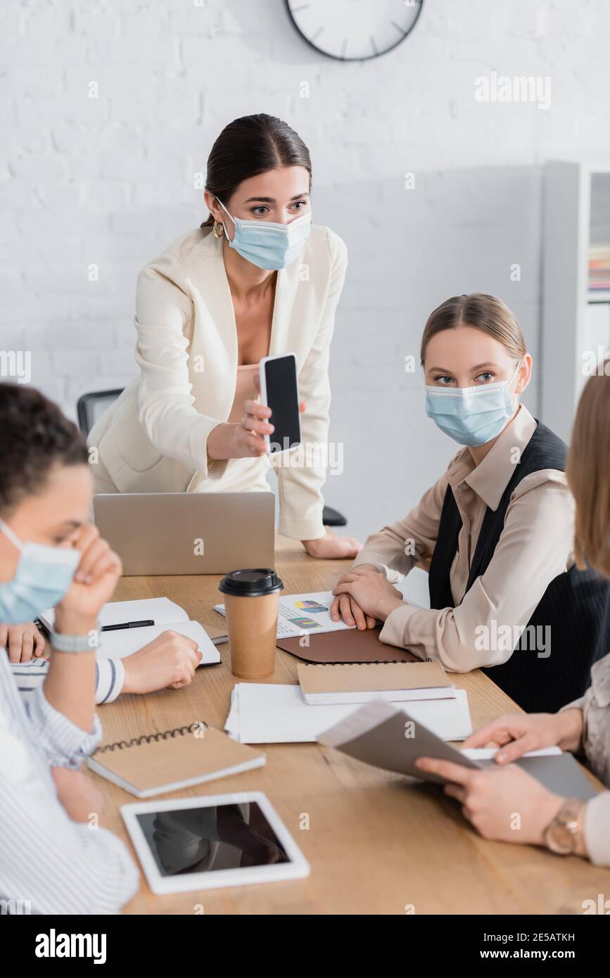 team leader in medical mask holding smartphone with blank screen near ...