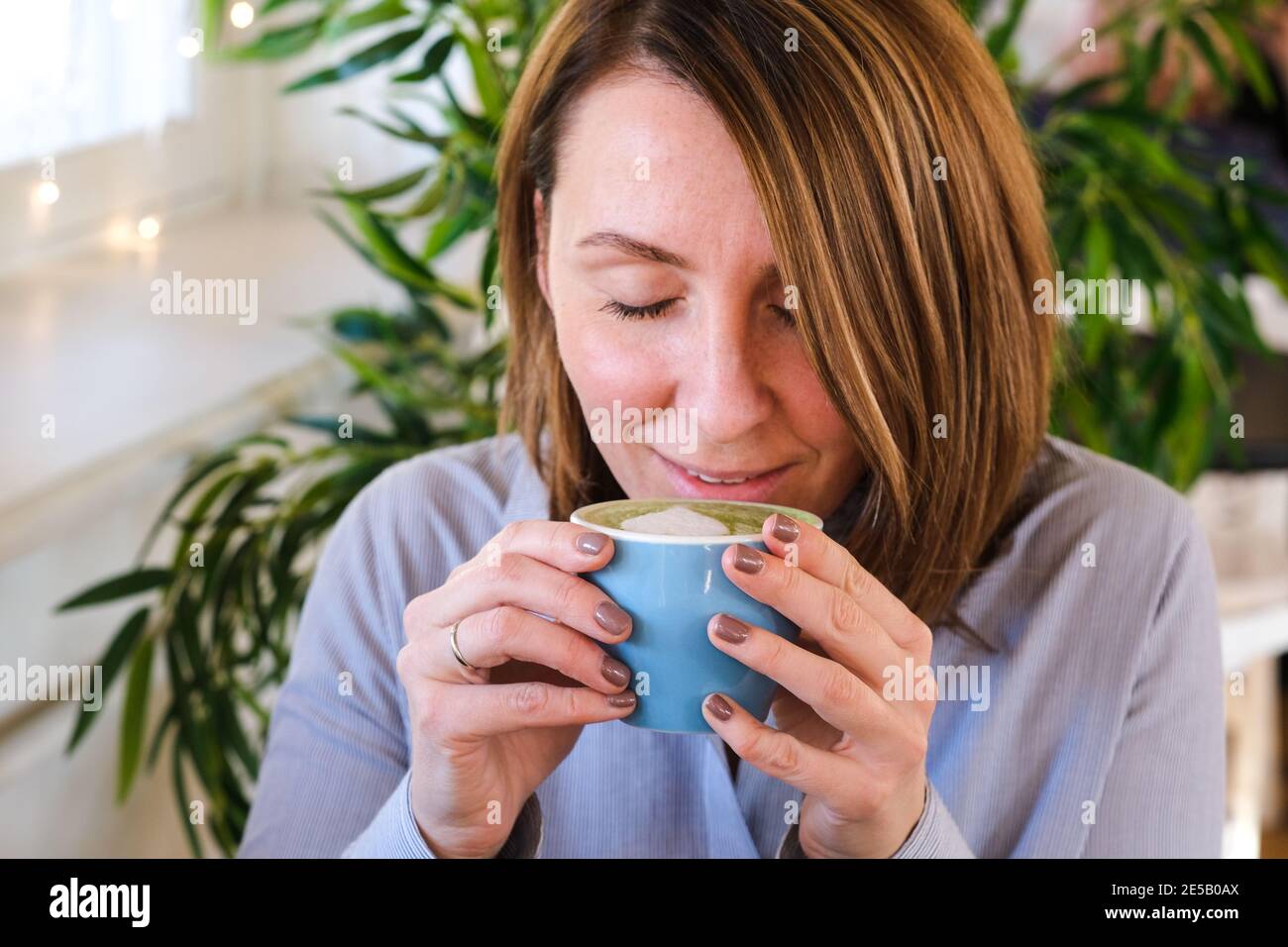 Young woman in cafe sipping matcha tea from a blue cup Stock Photo - Alamy