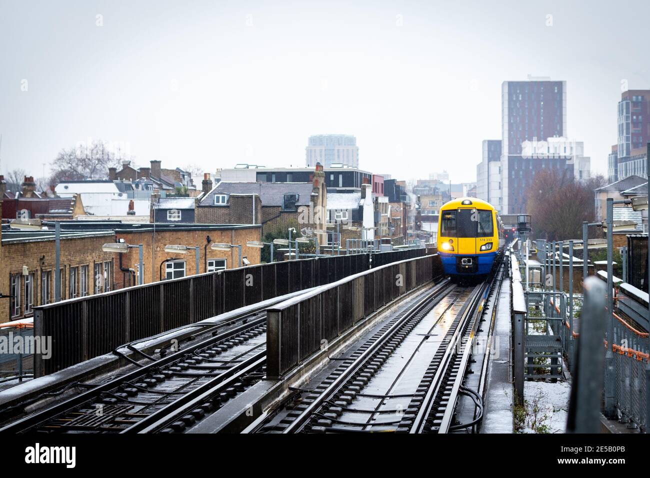 A Overground train approaches Haggerston station on a cold snowy day ...