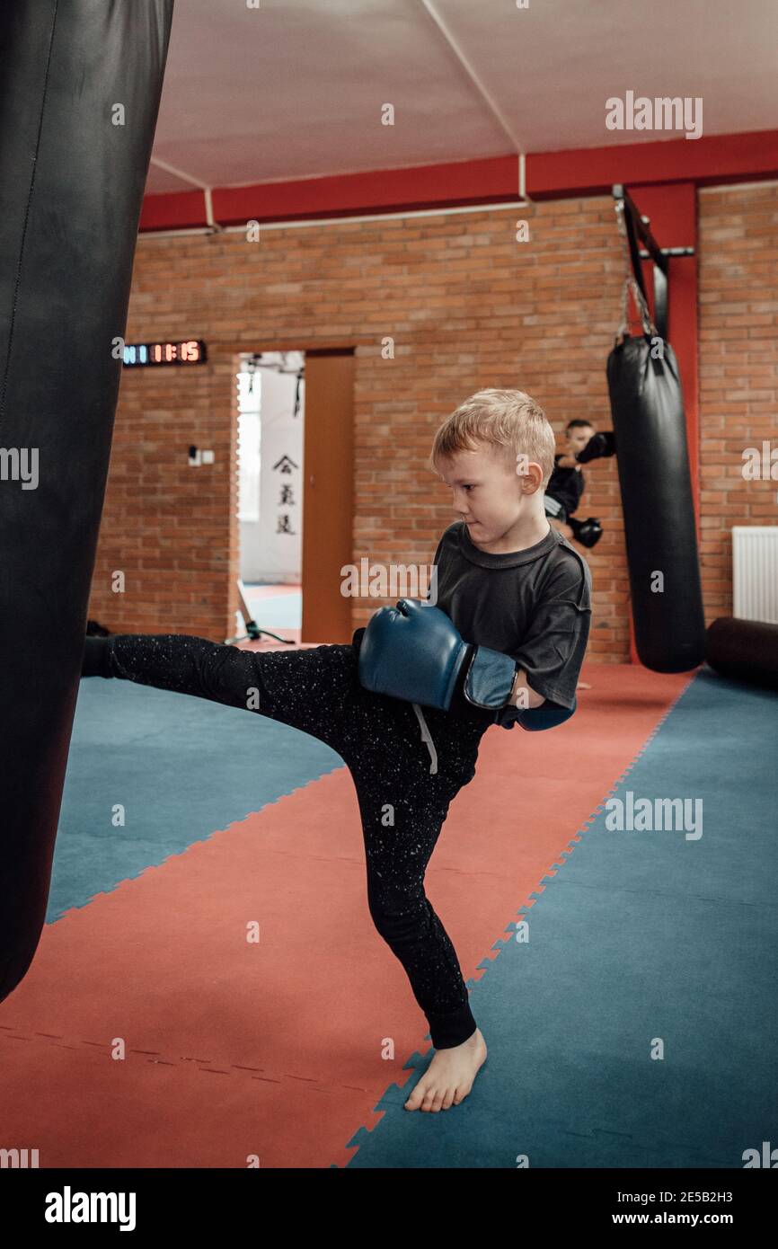 Portrait of a young boy kicking and punching a boxing bag in a gym ...