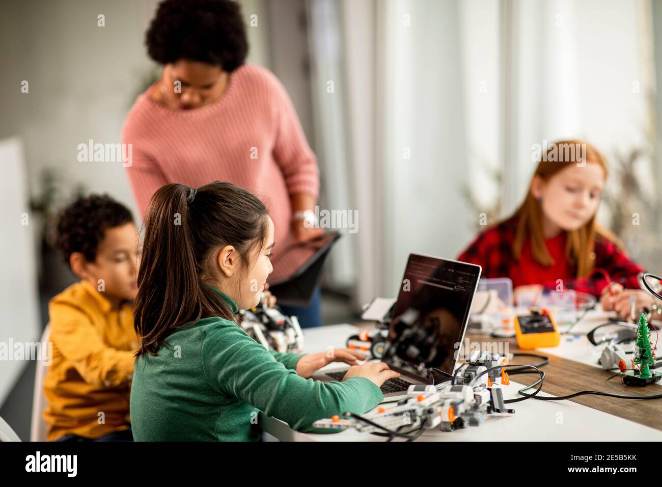 Group of happy kids with their African American female science teacher with laptop programming ...