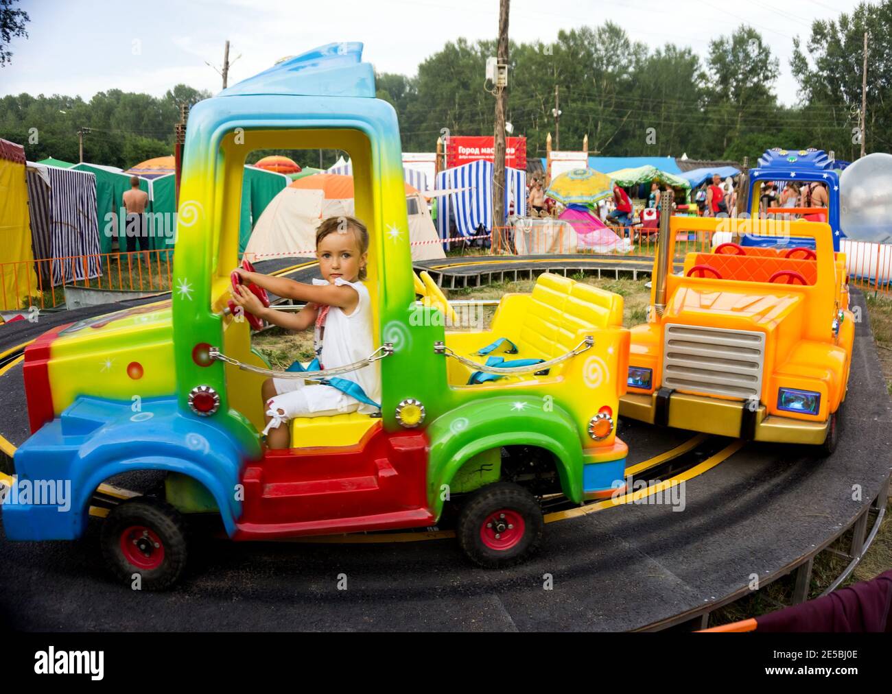 Little girl riding a carousel car on a summer day during the annual ...