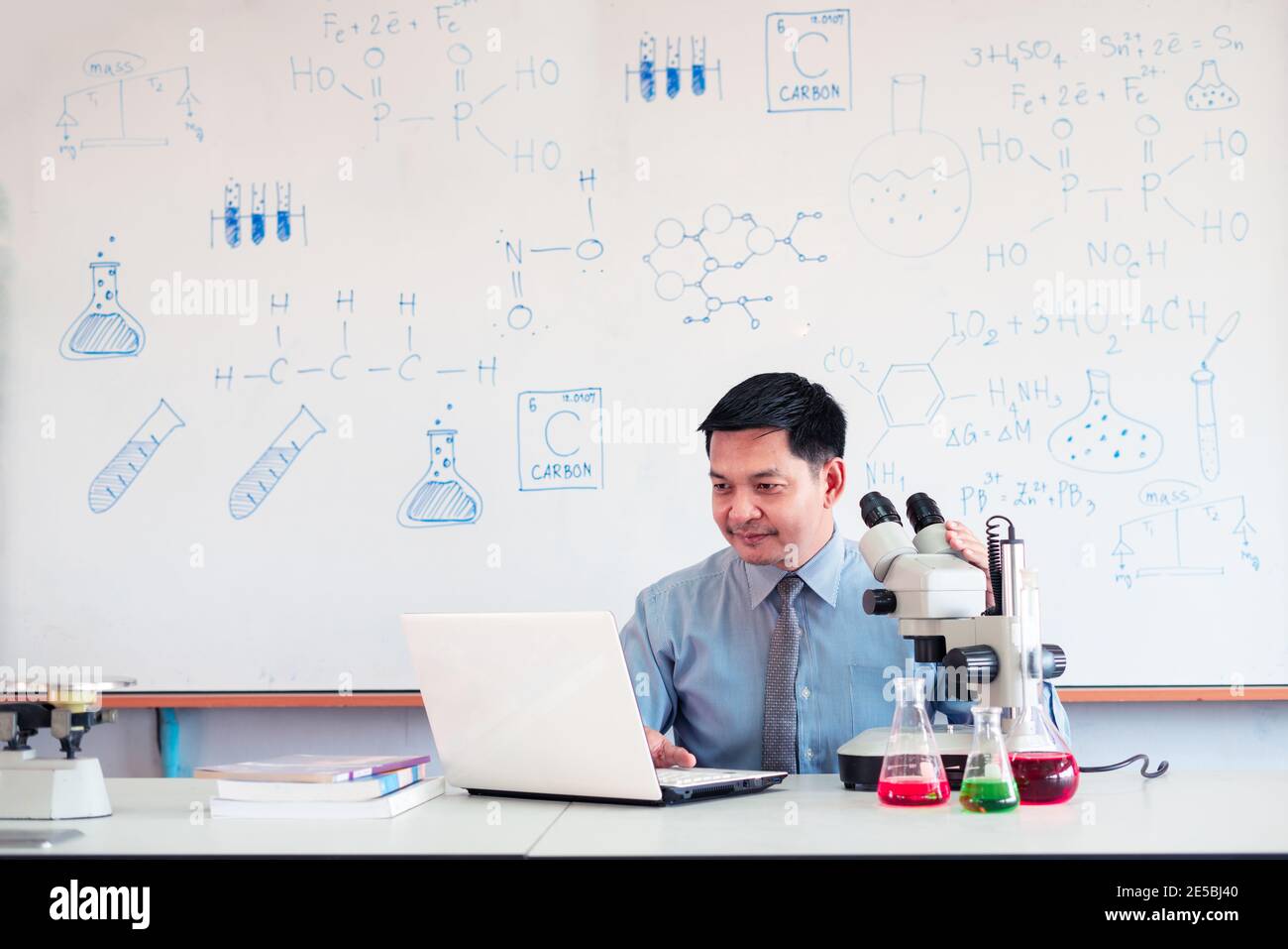 Science chemistry teacher teaching online with microscope and laptop in ...