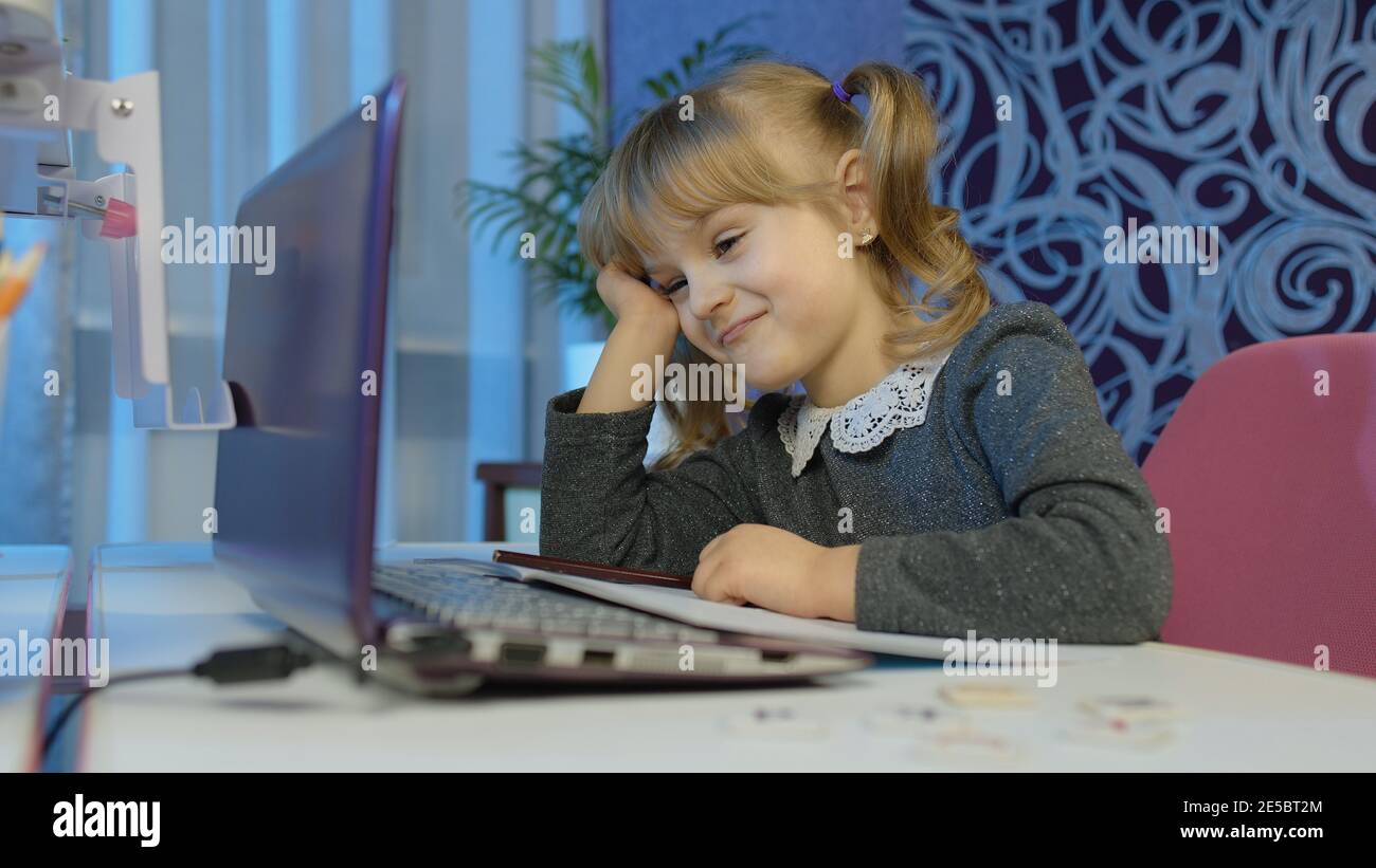 Bored kid listening audio lesson studying at table using digital laptop ...