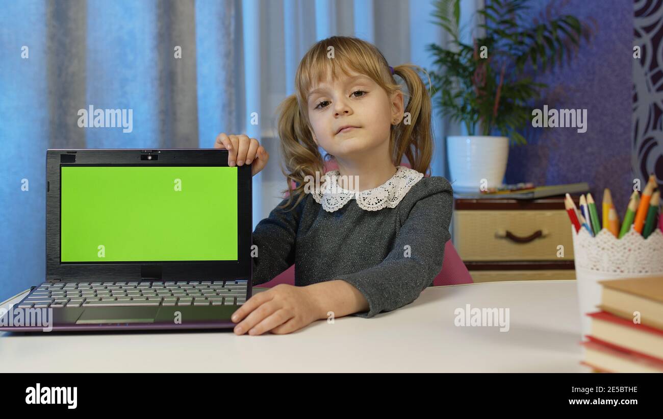 Child girl with laptop looking on chroma key pc green screen at home. E ...