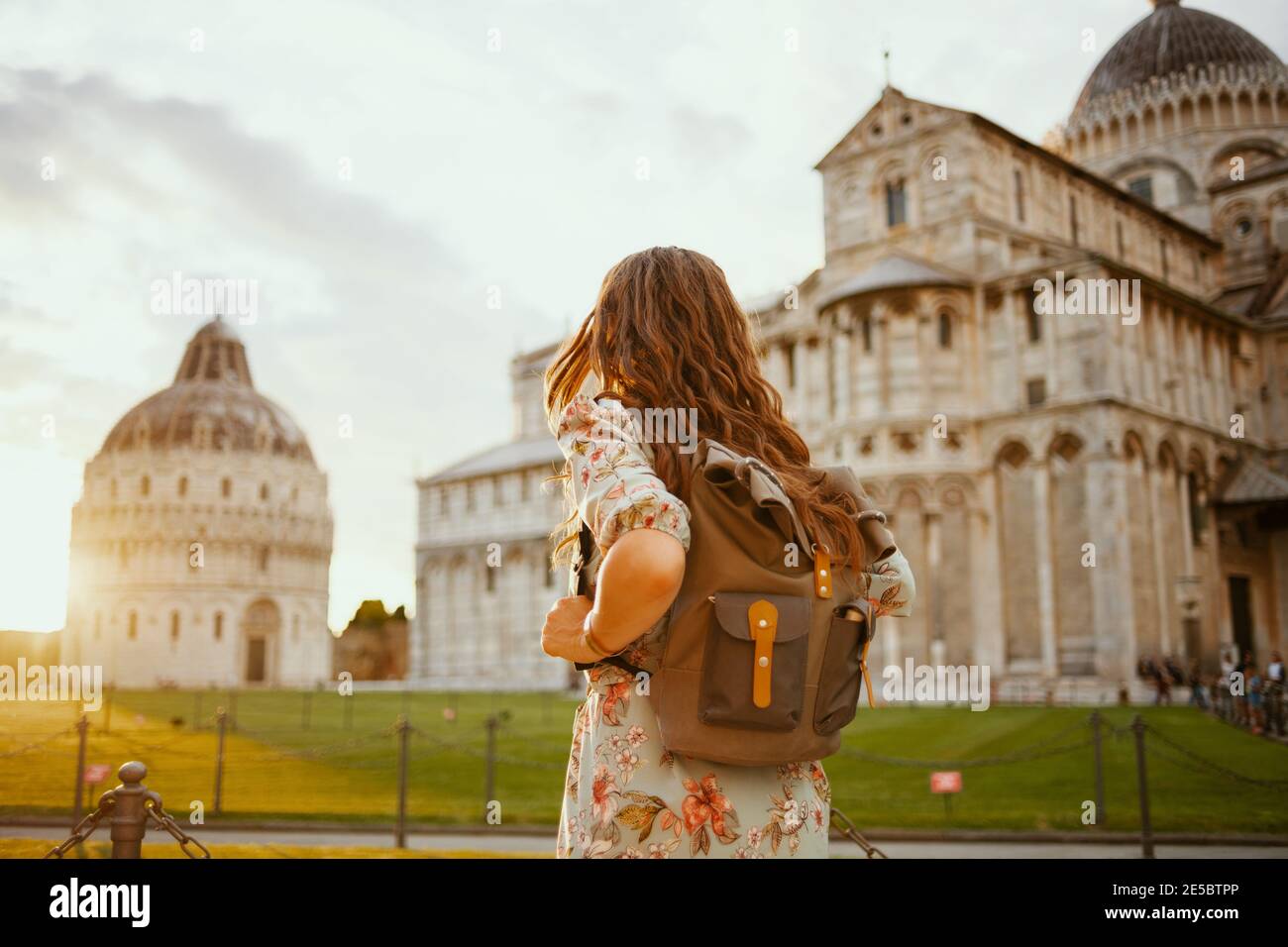 Seen from behind modern traveller woman in floral dress with backpack ...