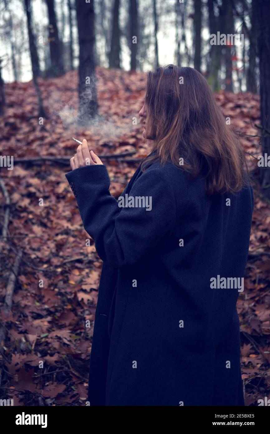 young brunette woman smoking cigarette in the forest in autumn Stock ...
