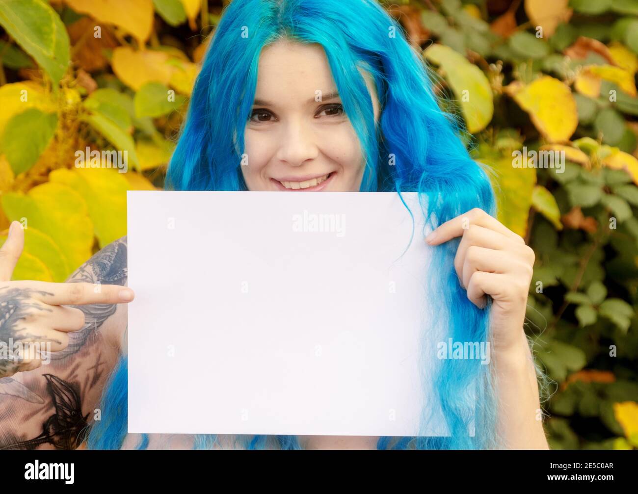 Beautiful young bohemian woman with blue hair happily holding a blank ...