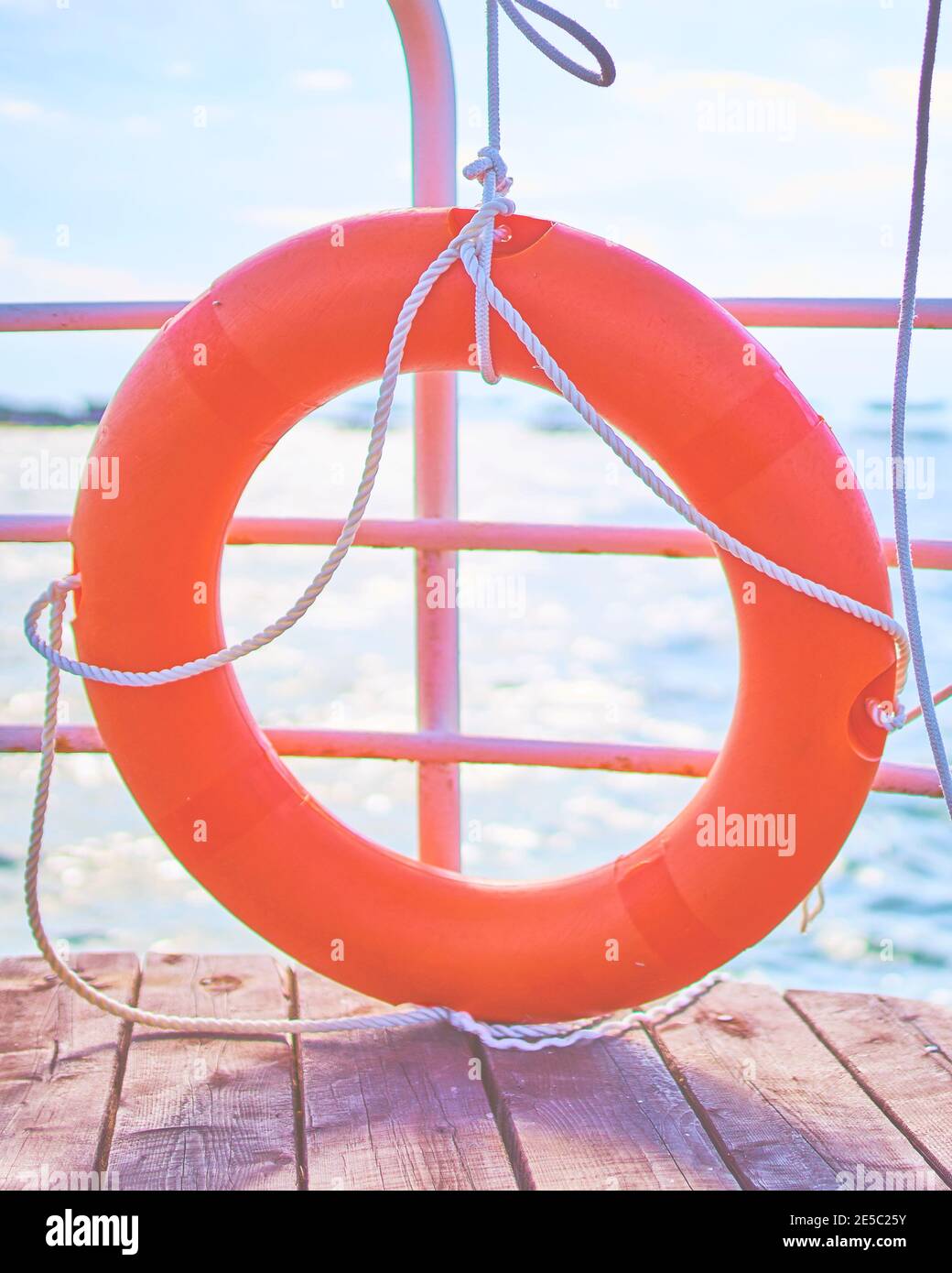Orange lifebuoy with a rope on a wooden pier by the sea. Equipment for rescuing drowning people ...