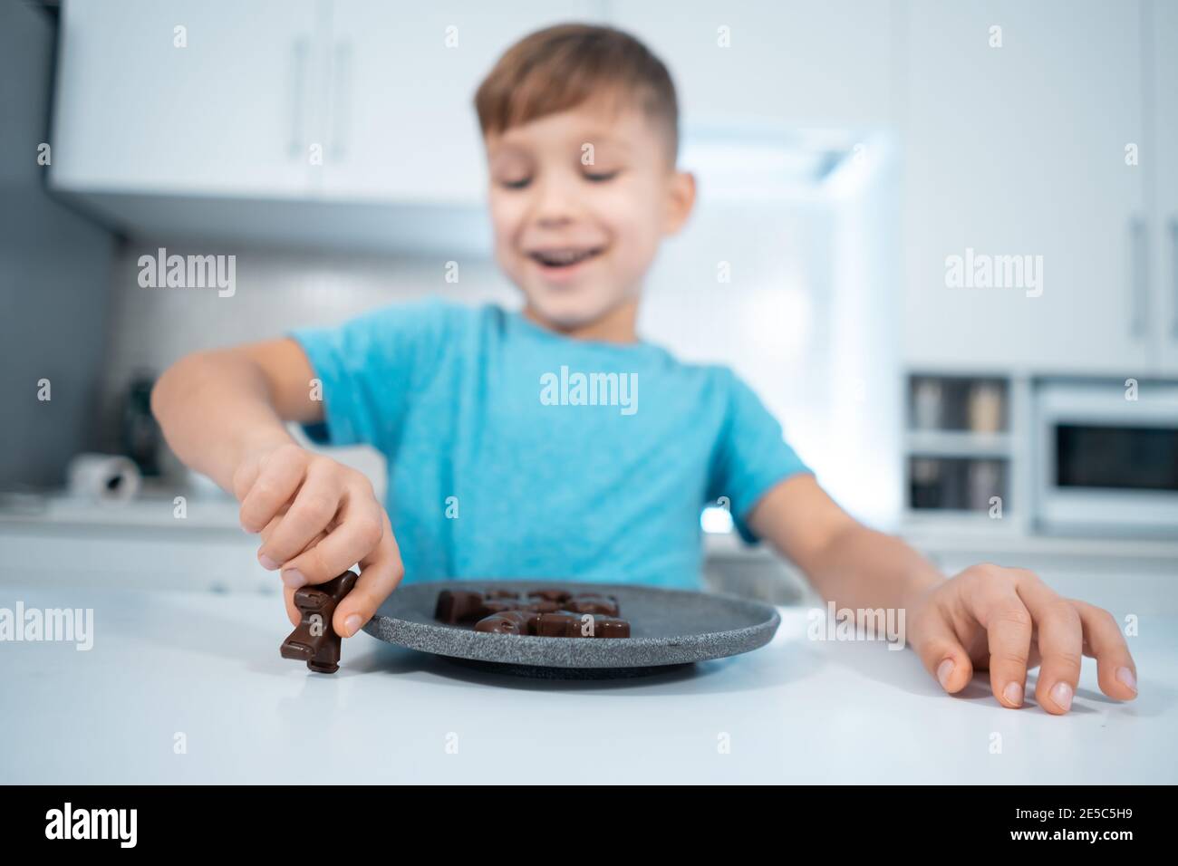 happy kid boy eating chocolate sweets and play candies at modern home ...
