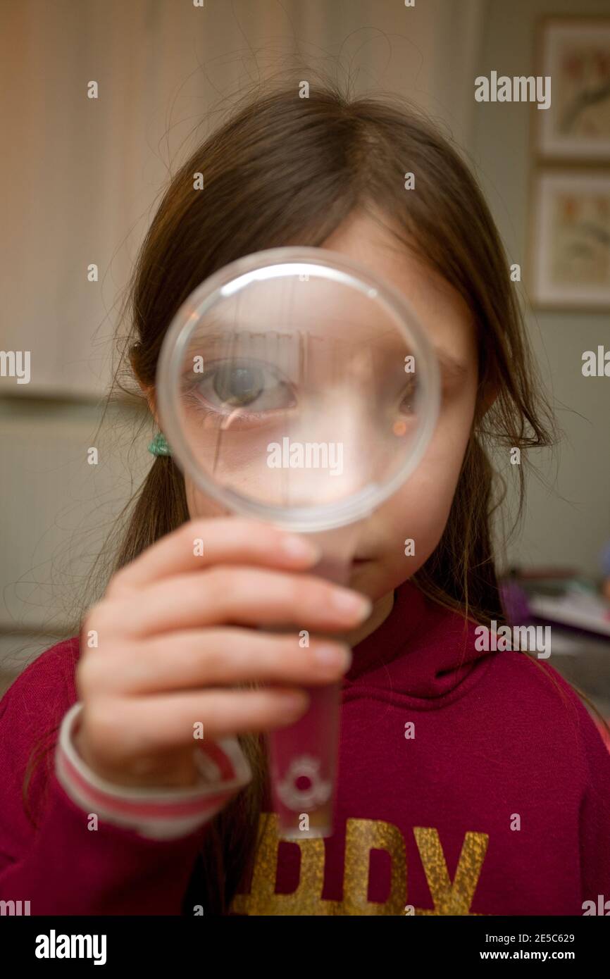 Young girl looking through magnifying glass Stock Photo - Alamy