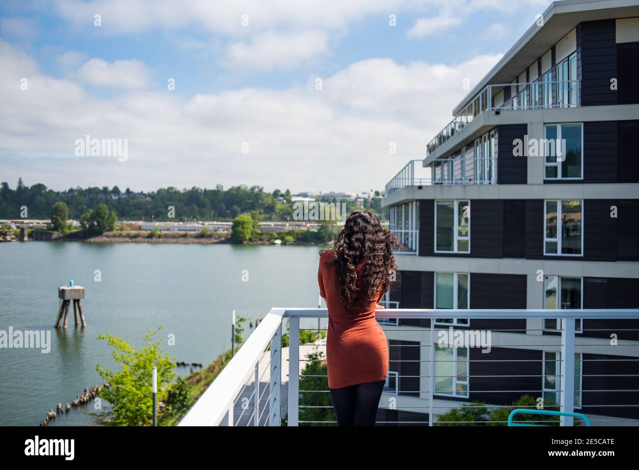 Woman looking out towards river on balcony with apartment building ...
