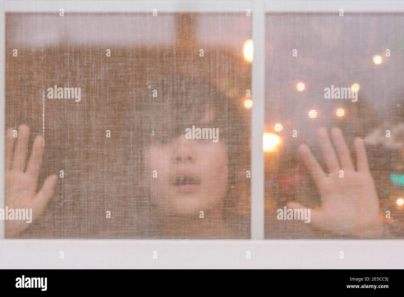 A young boy presses his face and hands up to a screened window Stock ...