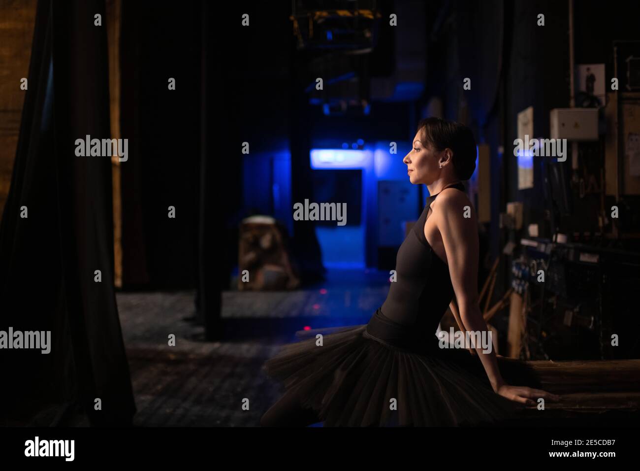 Adult female ballet dancer leaning back while sitting behind stage ...