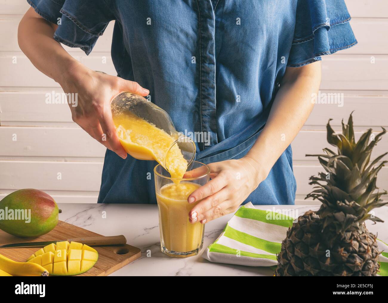 Young woman pouring pineapple and mango smoothie into glass. Healthy ...