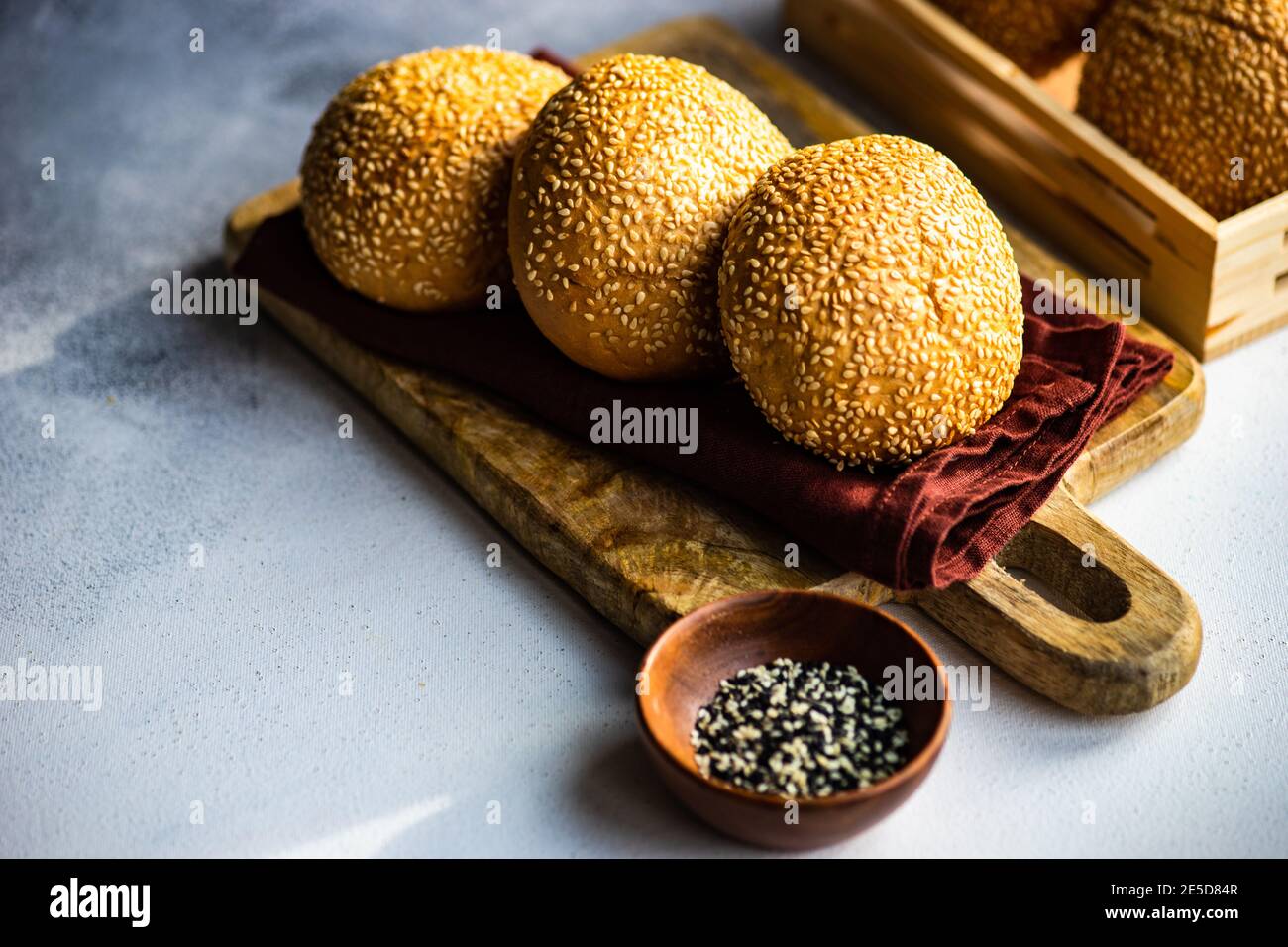 Bread rolls on a chopping board with a bowl of sesame seeds Stock Photo ...