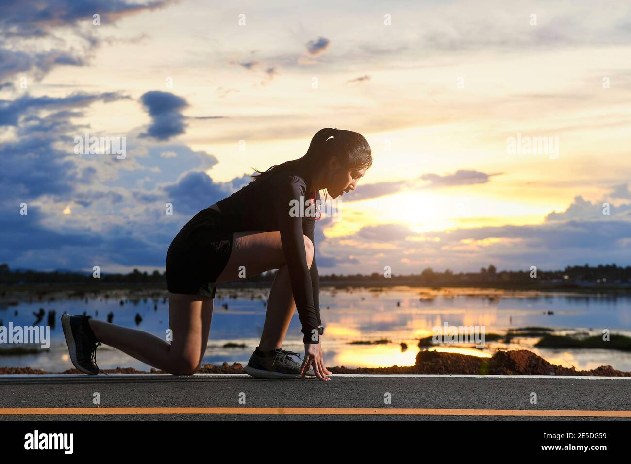 Woman getting ready to run along a lakeside road, Thailand Stock Photo ...
