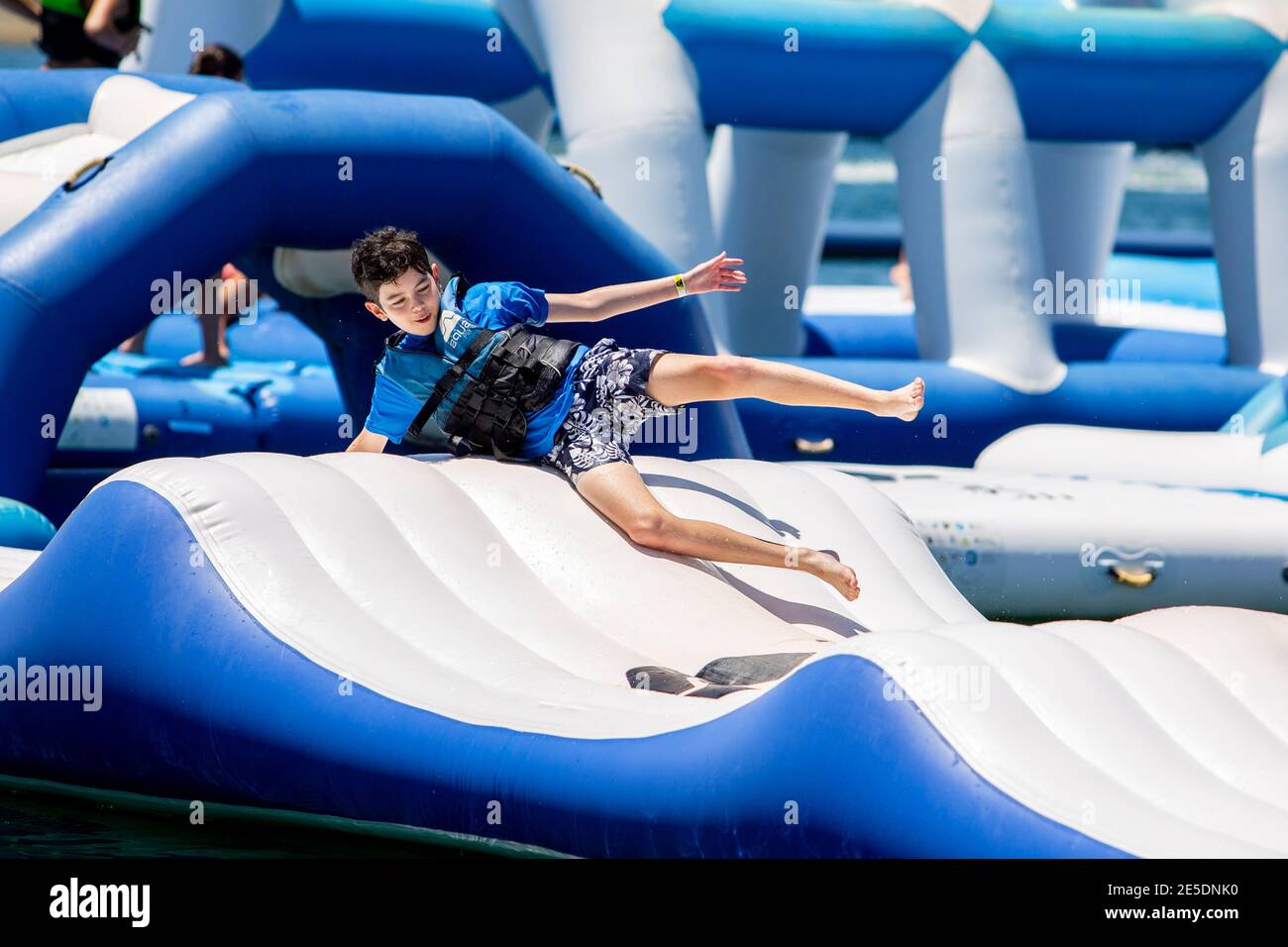 A boy playing at a water park, jumping over inflatable obstacle ...