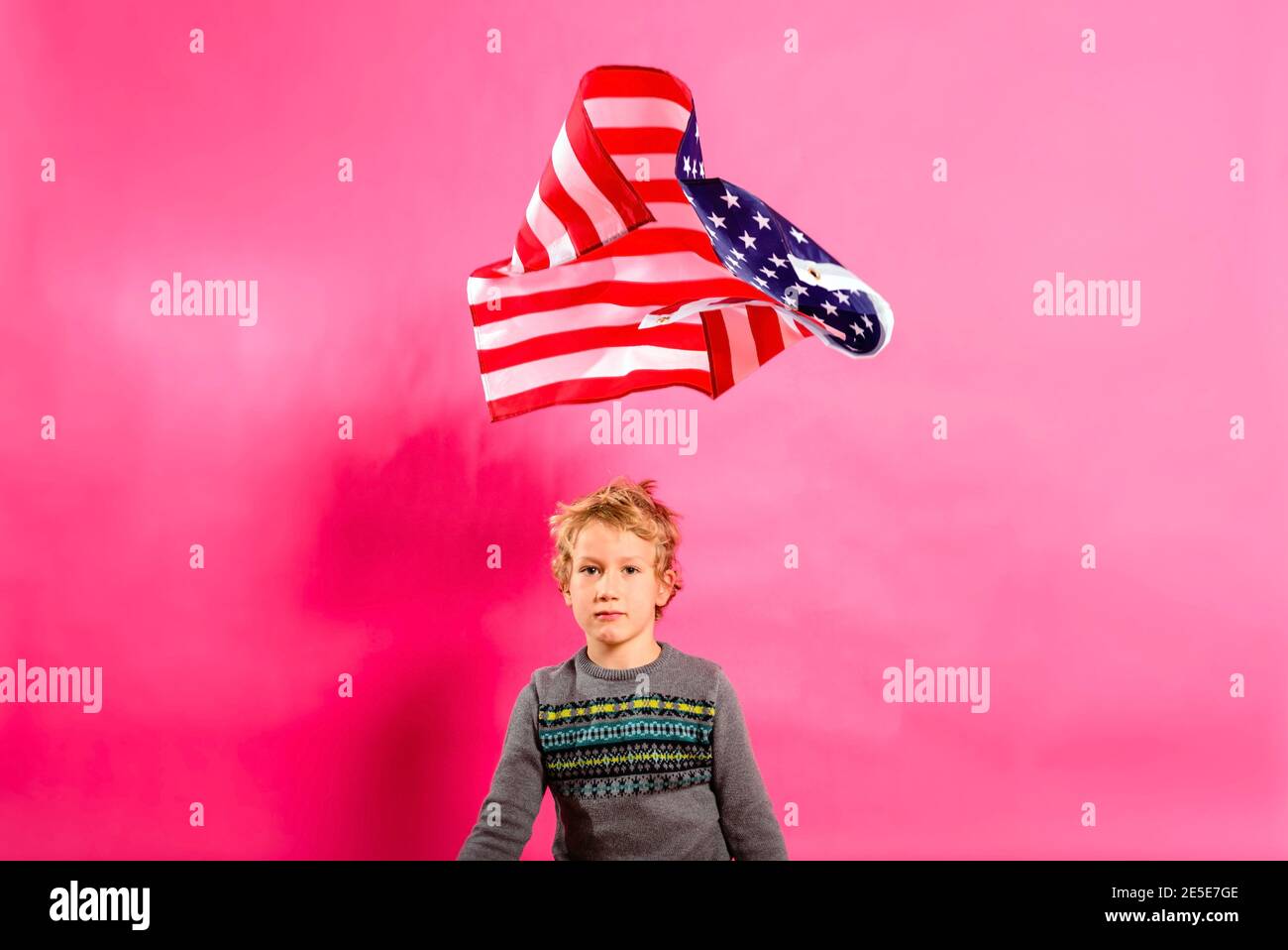 Blond boy under a floating American flag, isolated on a pink background ...
