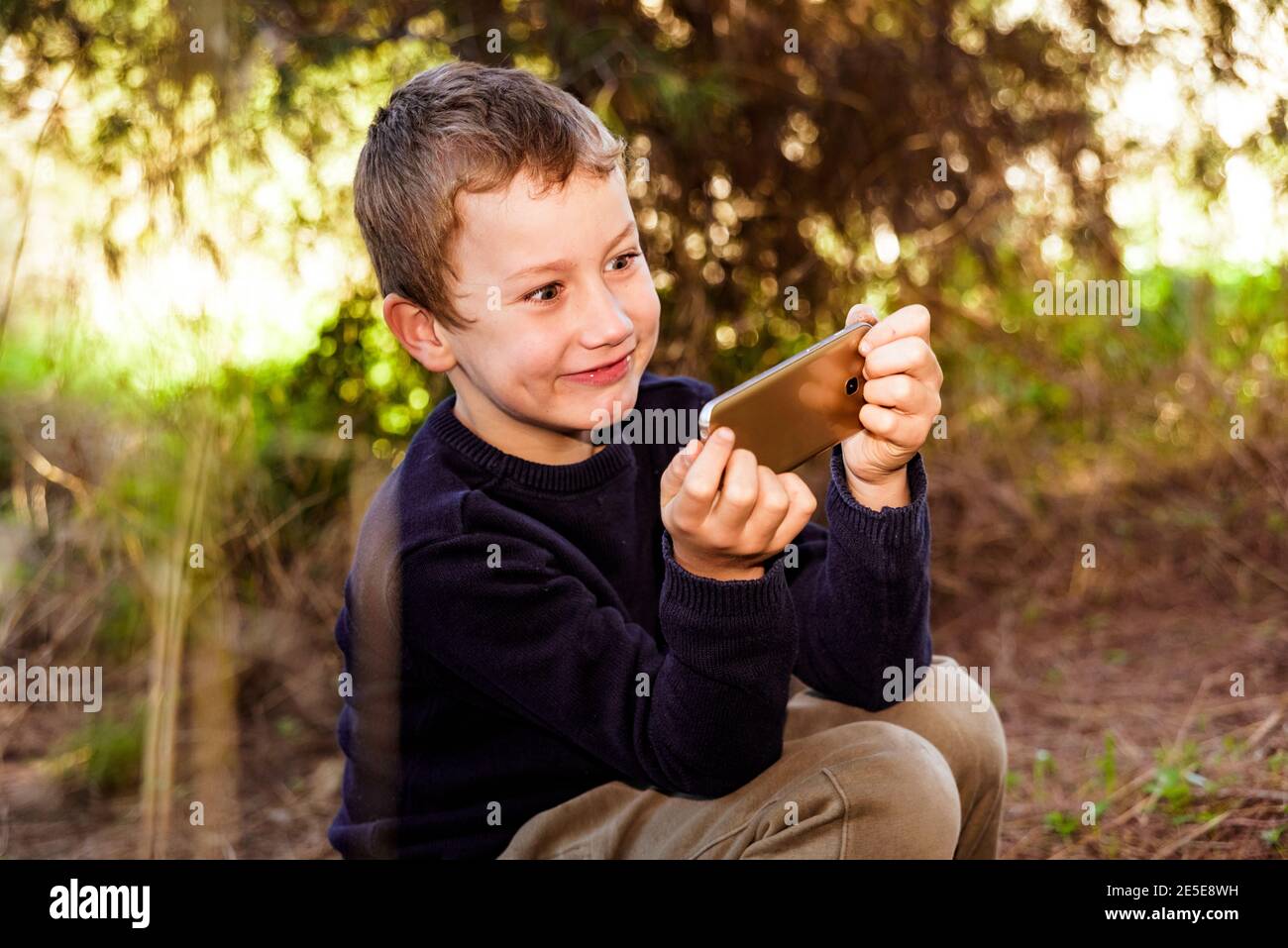 Happy child plays with his mobile phone during an excursion to nature ...