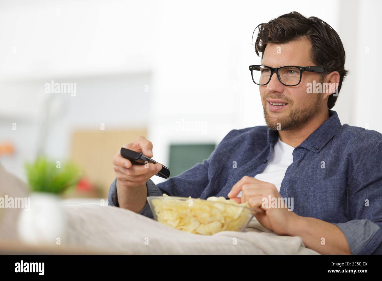 man sitting on the sofa watching tv and eating chips Stock Photo - Alamy