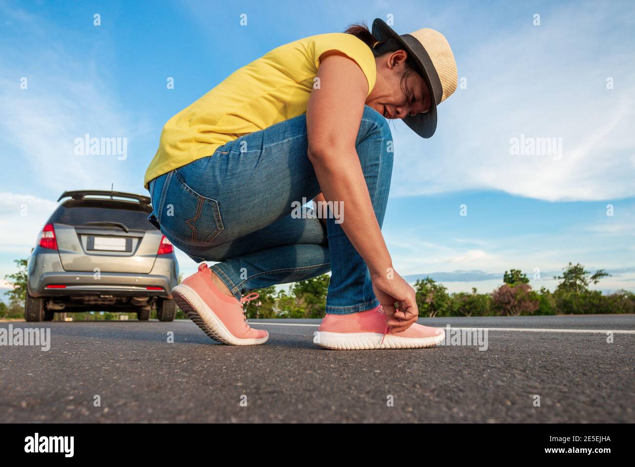 Women wearing jeans binding sneakers on the highway, car parked along ...
