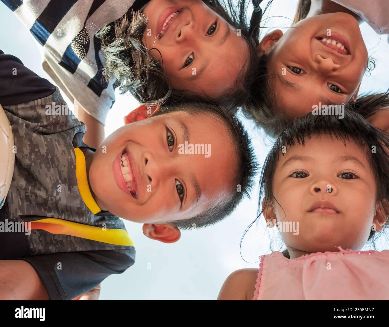 Low angle shot of excited children stand in circle hugging looking at camera at playing together ...