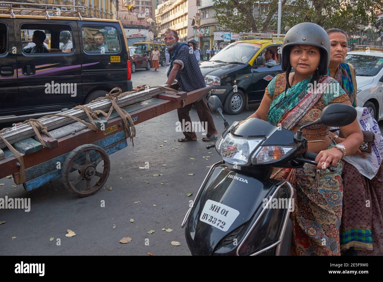 A woman with her pillion rider driving her scooter through busy ...